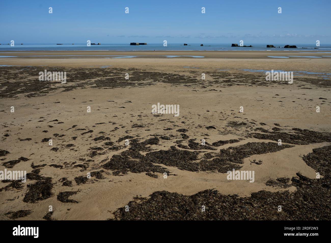 Gold Beach with the remains of WW2 Mulberry Harbour in the sea behind ...