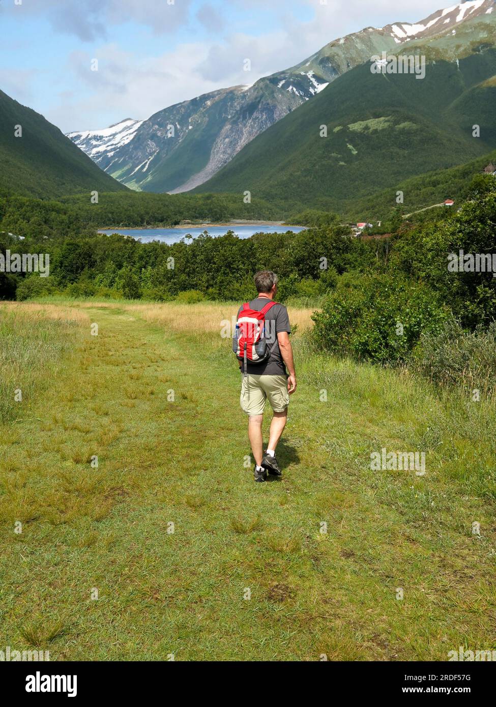 Man walking on grassy path in between mountains Stock Photo - Alamy