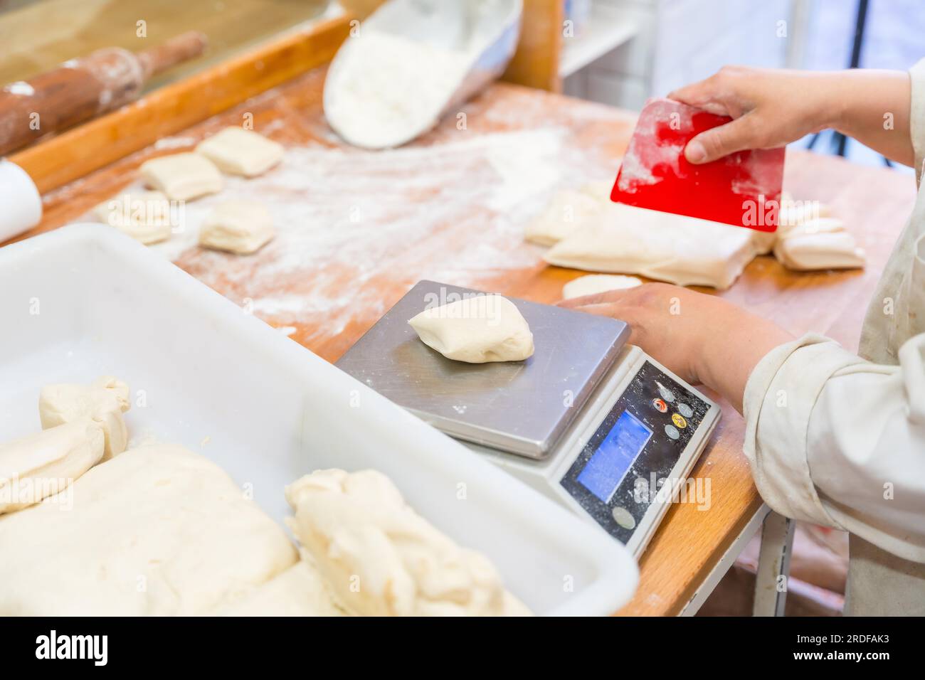 Woman bread maker employee in artisan bakery workshop cutting dough for ...