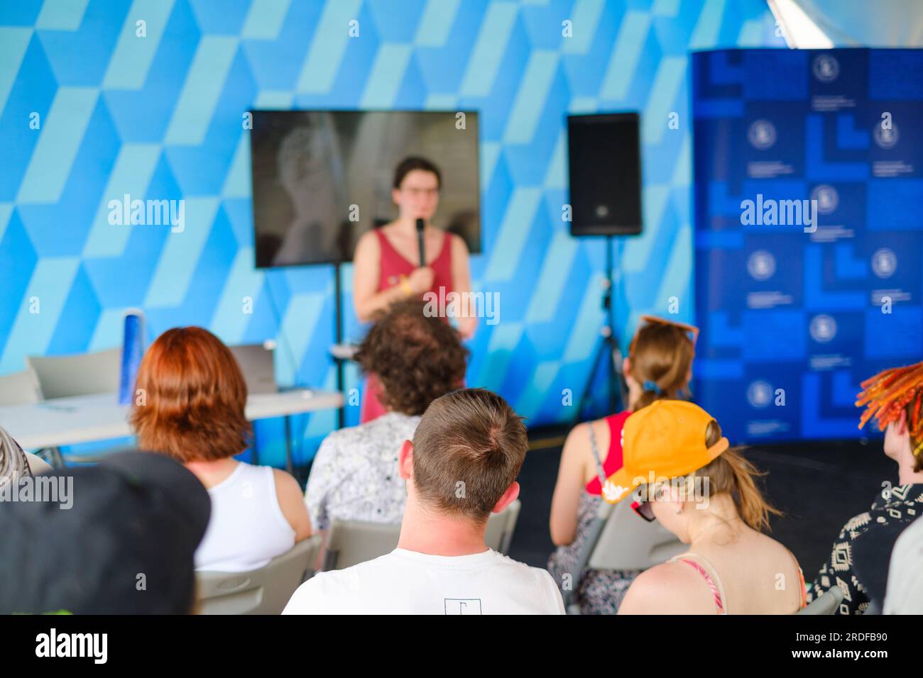 Blurred female with microphone giving lecture to audience from stage ...