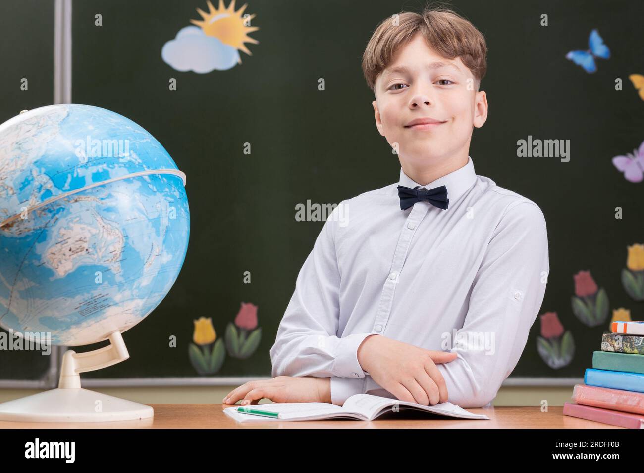 A beautiful happy schoolboy is sitting at a desk on the background of a ...