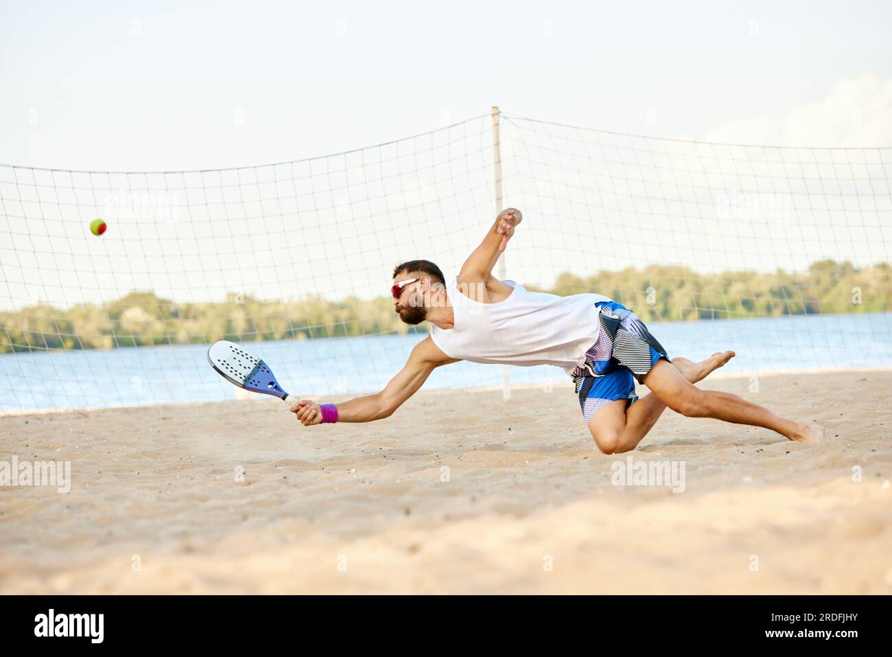Dynamic image of young man playing beach, paddle tennis, hitting ball ...