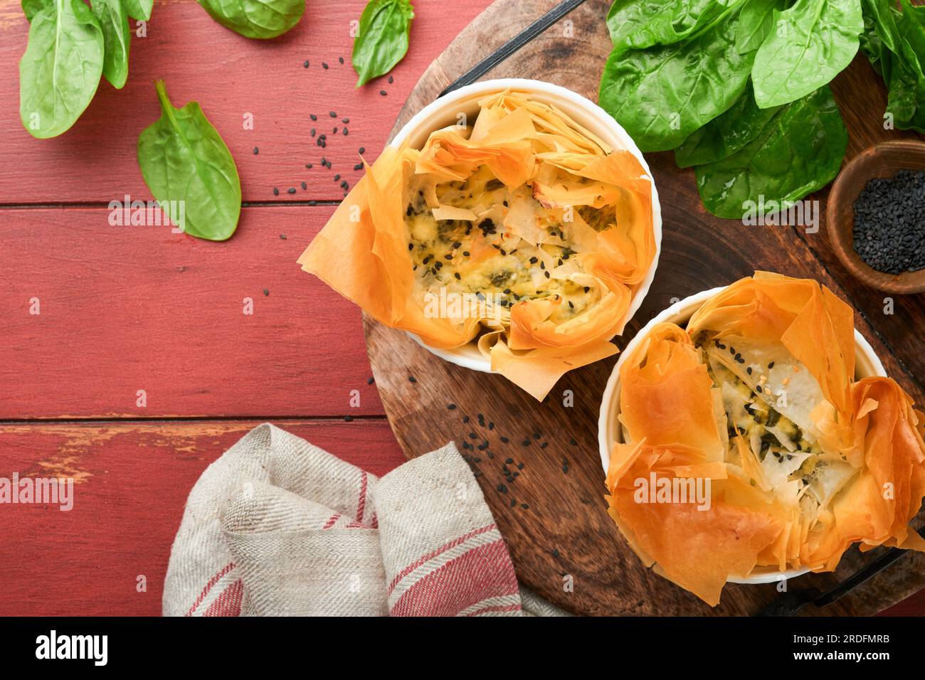 Filo pies with soft feta cheese and spinach in ceramic molds on old red ...