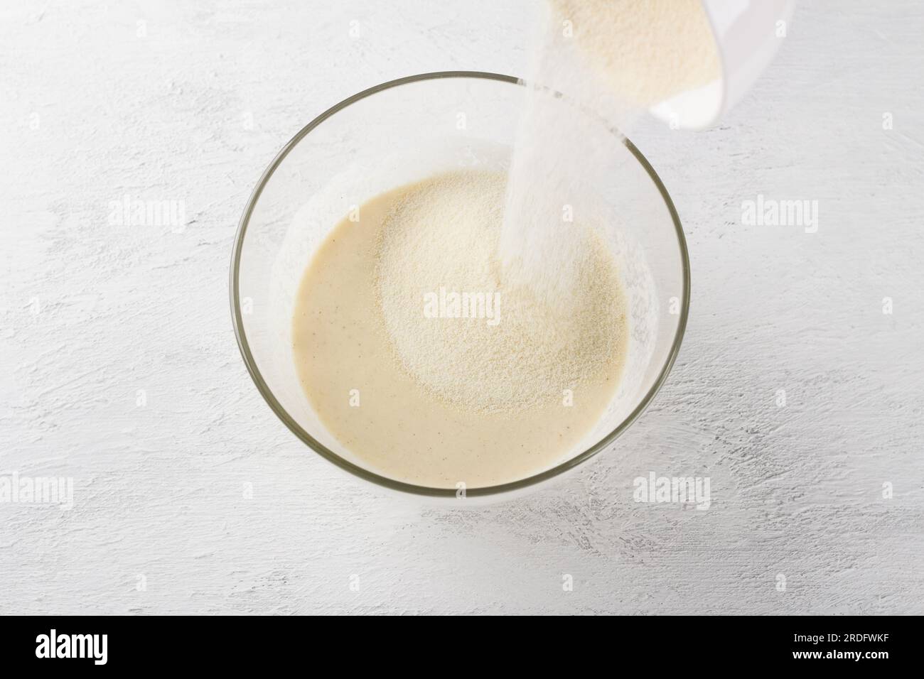 Raw semolina is pouring in a glass bowl with a creamy egg previously ...