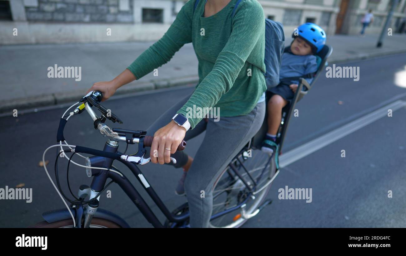 Cyclist mother riding bicycle in street with toddler in back seat Stock ...
