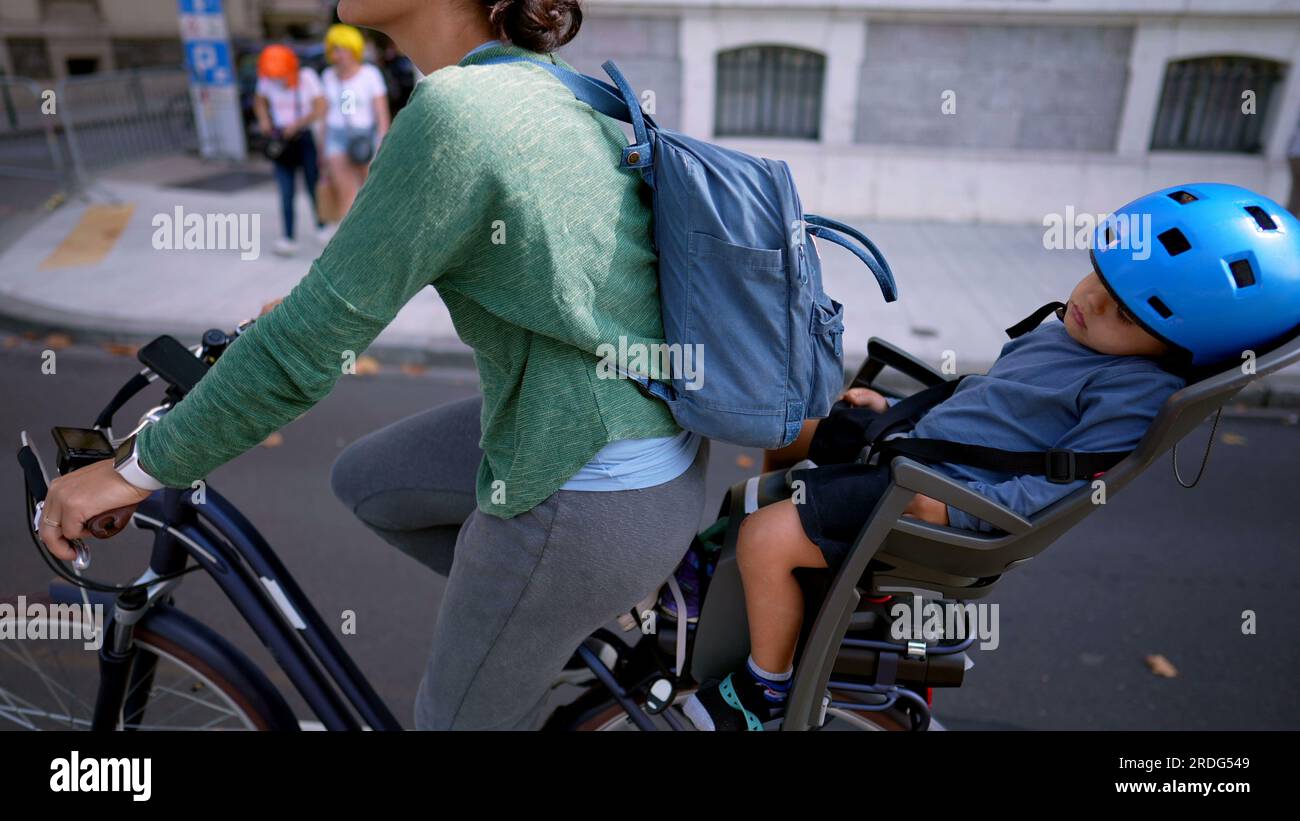 Happy woman riding bicycle with sleeping child in back seat in urban ...