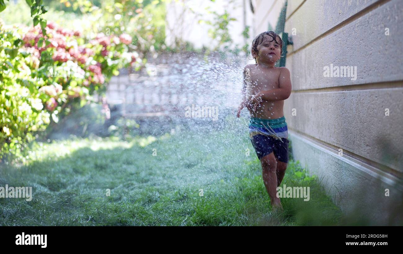 little boy having fun running under water spraying hose in garden ...
