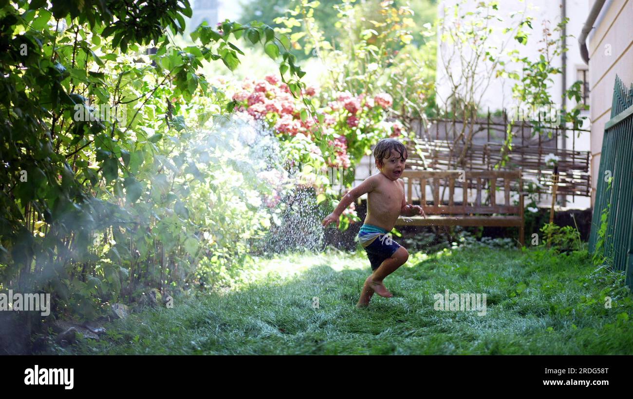 little boy having fun running under water spraying hose in garden ...