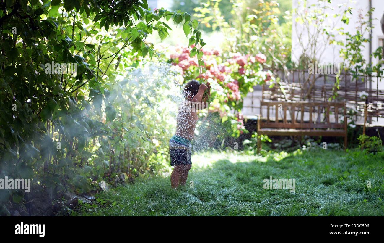 little boy having fun running under water spraying hose in garden ...