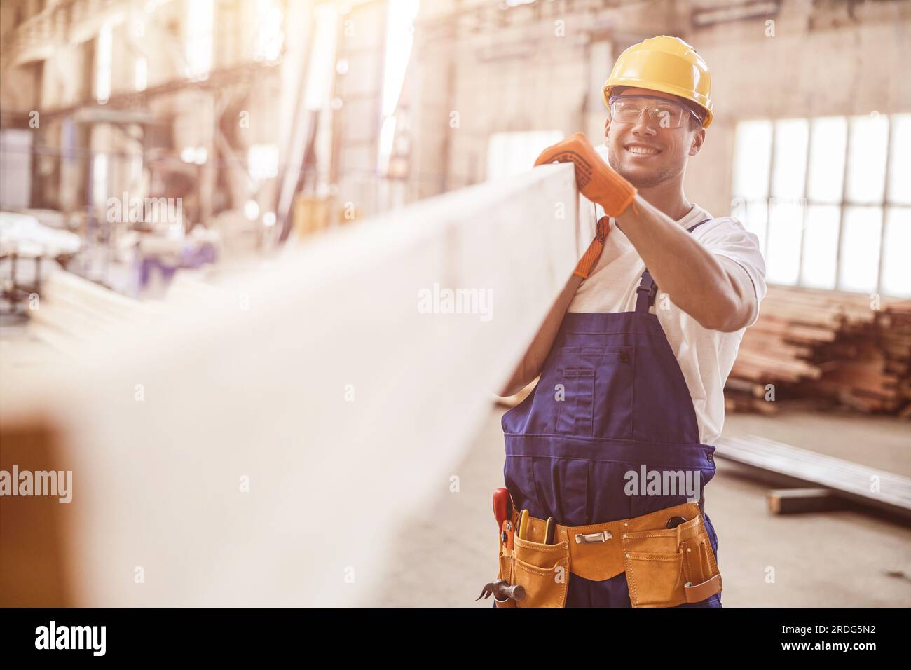 Smiling man builder carrying wooden plank at construction site Stock ...