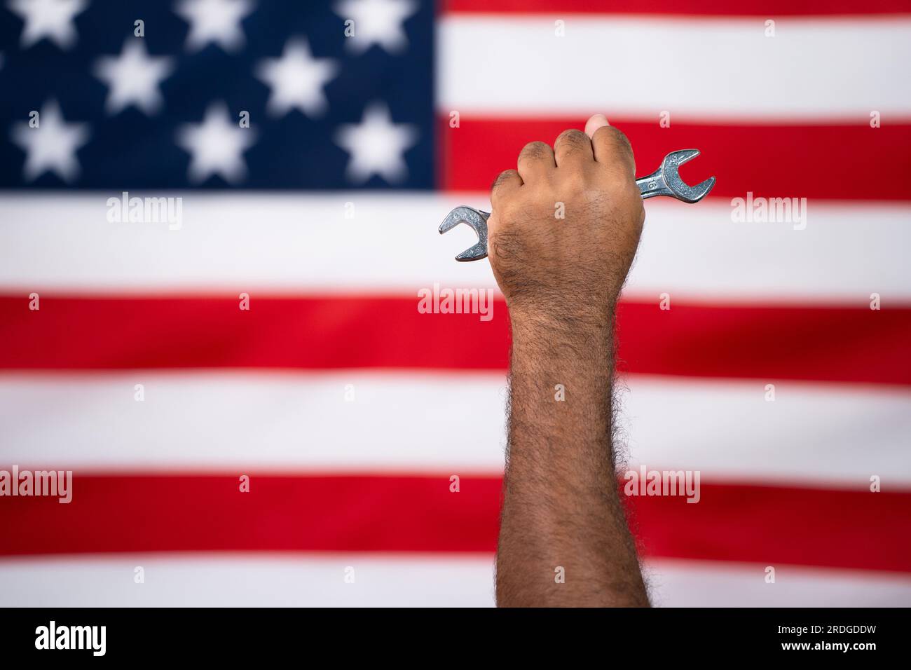 Close up shot of labour raising hand by holding spanner in front of US ...