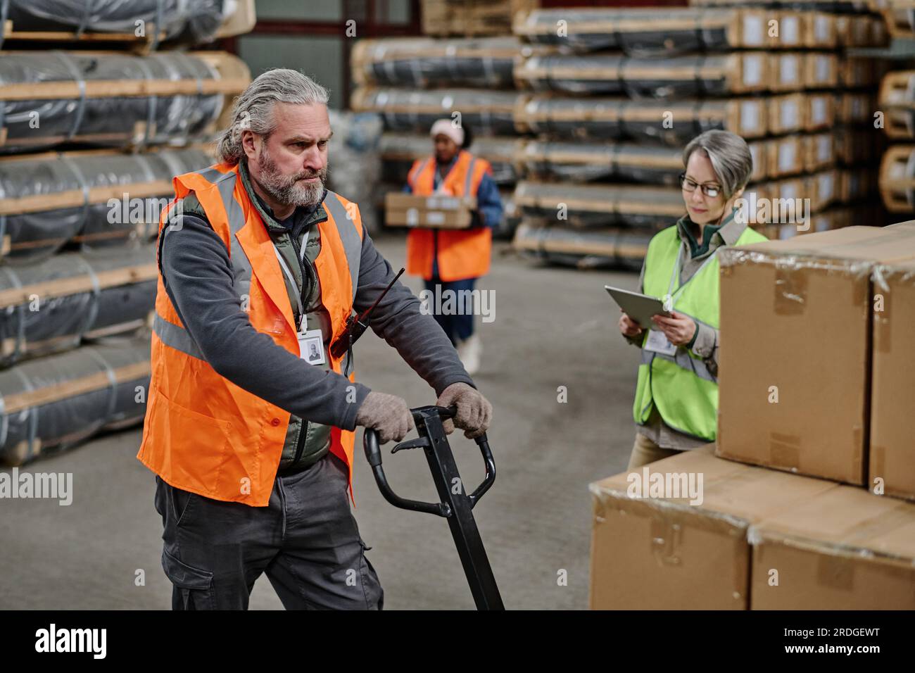 Mature worker in protective workwear loading cargo with loader in ...