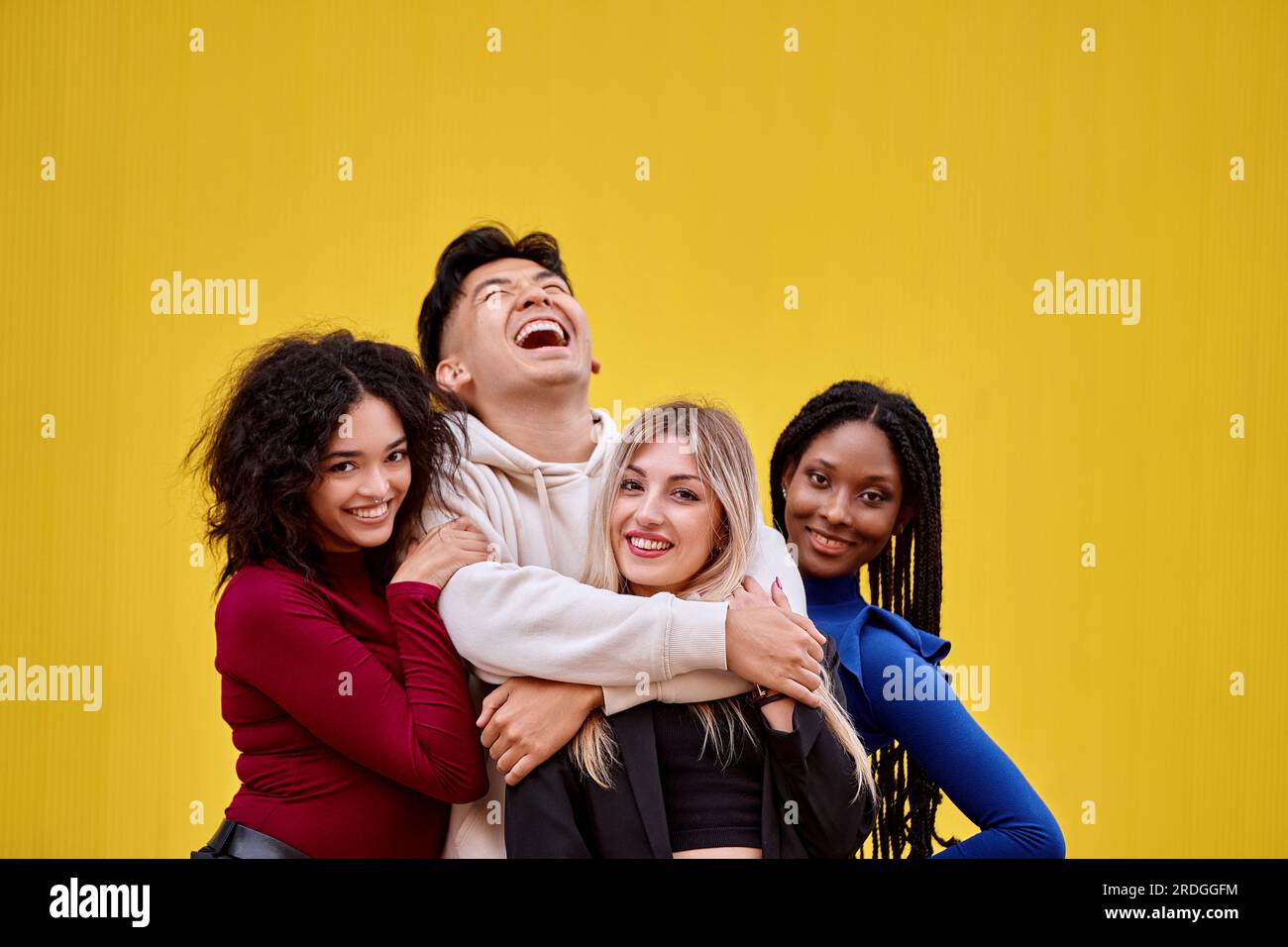 Happy multi-ethnic friends posing together in front of a yellow wall ...
