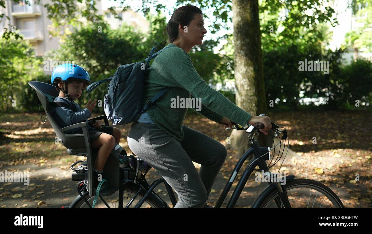 Parent riding bicycle with little boy in bike back seat mother rides ...
