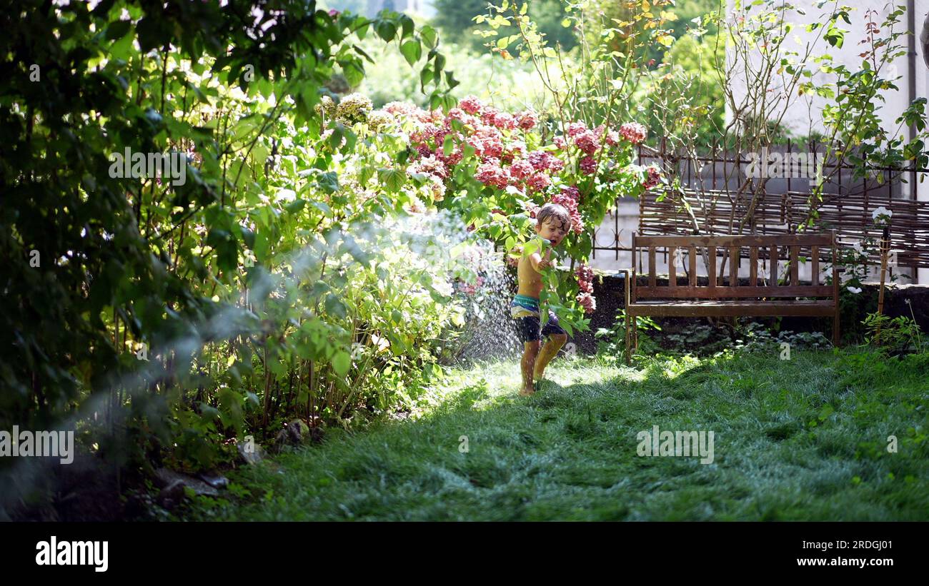 Splashing water into little boy outside in home garden during hot ...