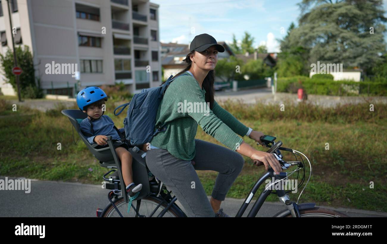 Mother riding bicycle with child in back seat outside in urban green ...