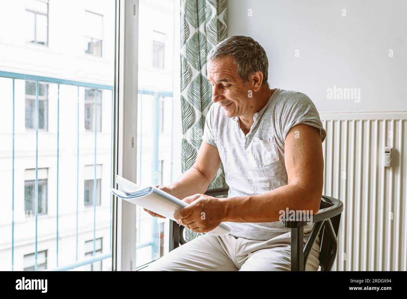 man sitting at window reading folder with documents Stock Photo - Alamy