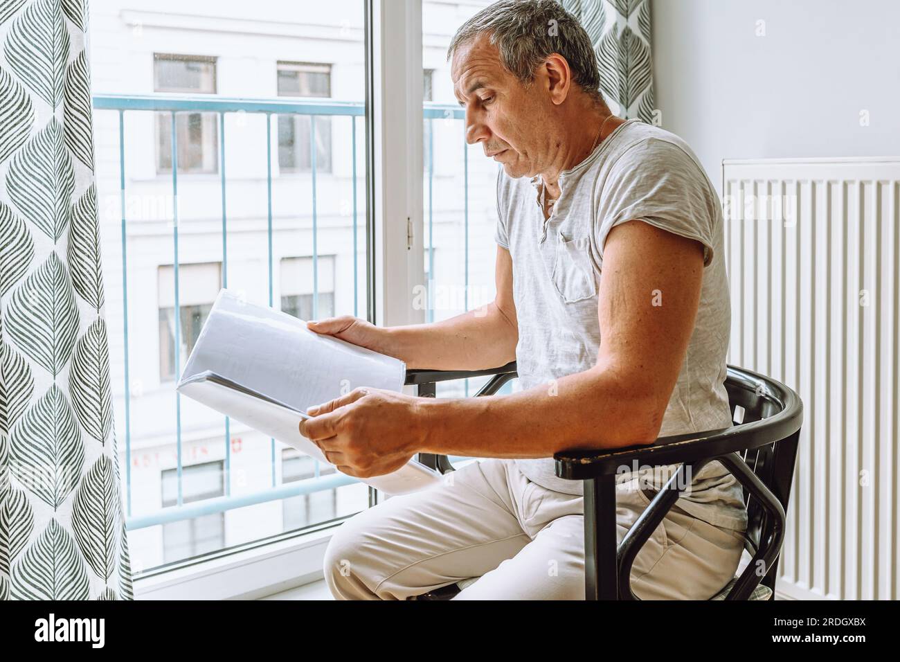 man sitting at window reading folder with documents Stock Photo - Alamy