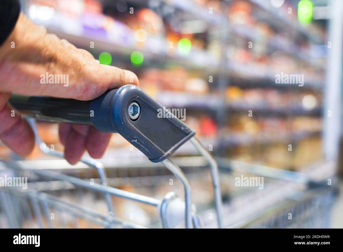 An older man's hand pushing a cart in a supermarket, blurred background ...