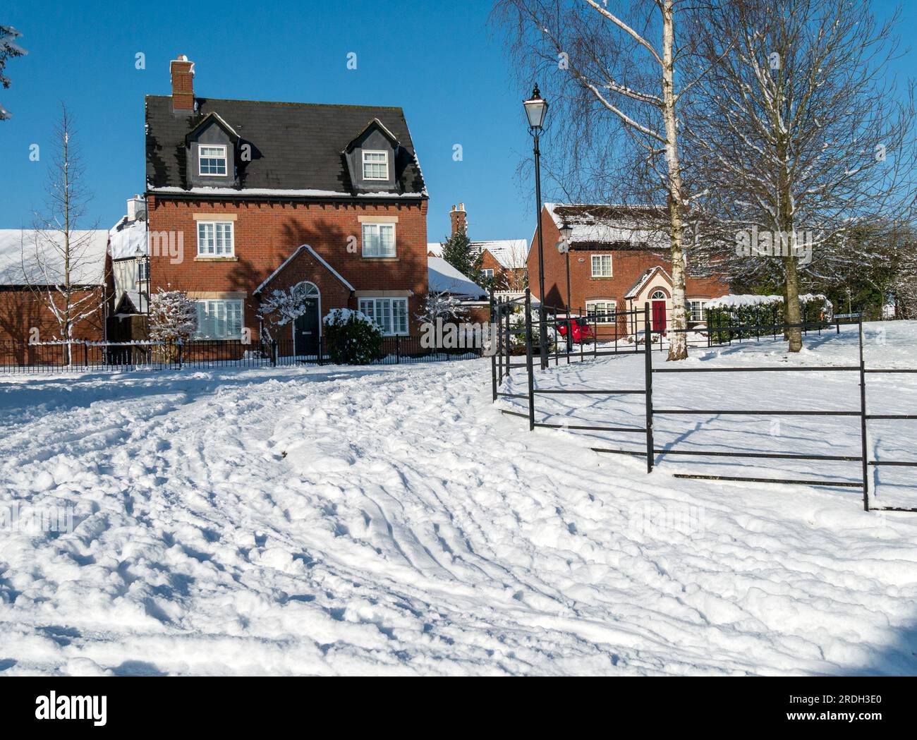 Snow covered road with tyre tracks and footprints on housing estate in Winter, Leicestershire ...