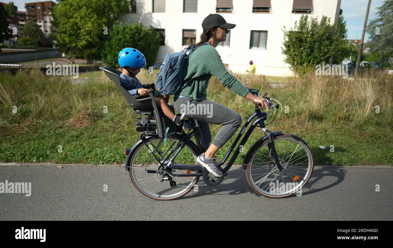 Parent riding bicycle with child sitting in back seat Stock Photo - Alamy