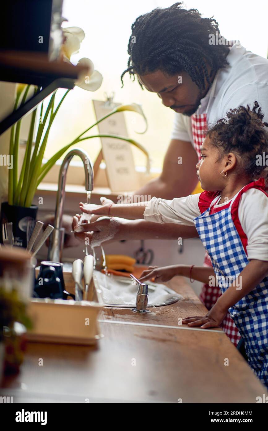 Young father washing dishes with her little daughter in a domestic ...
