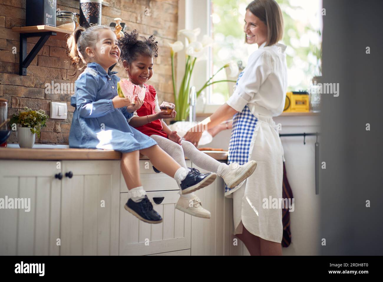 Two adorable little girls sitting on kitchen counter eating watermelon ...