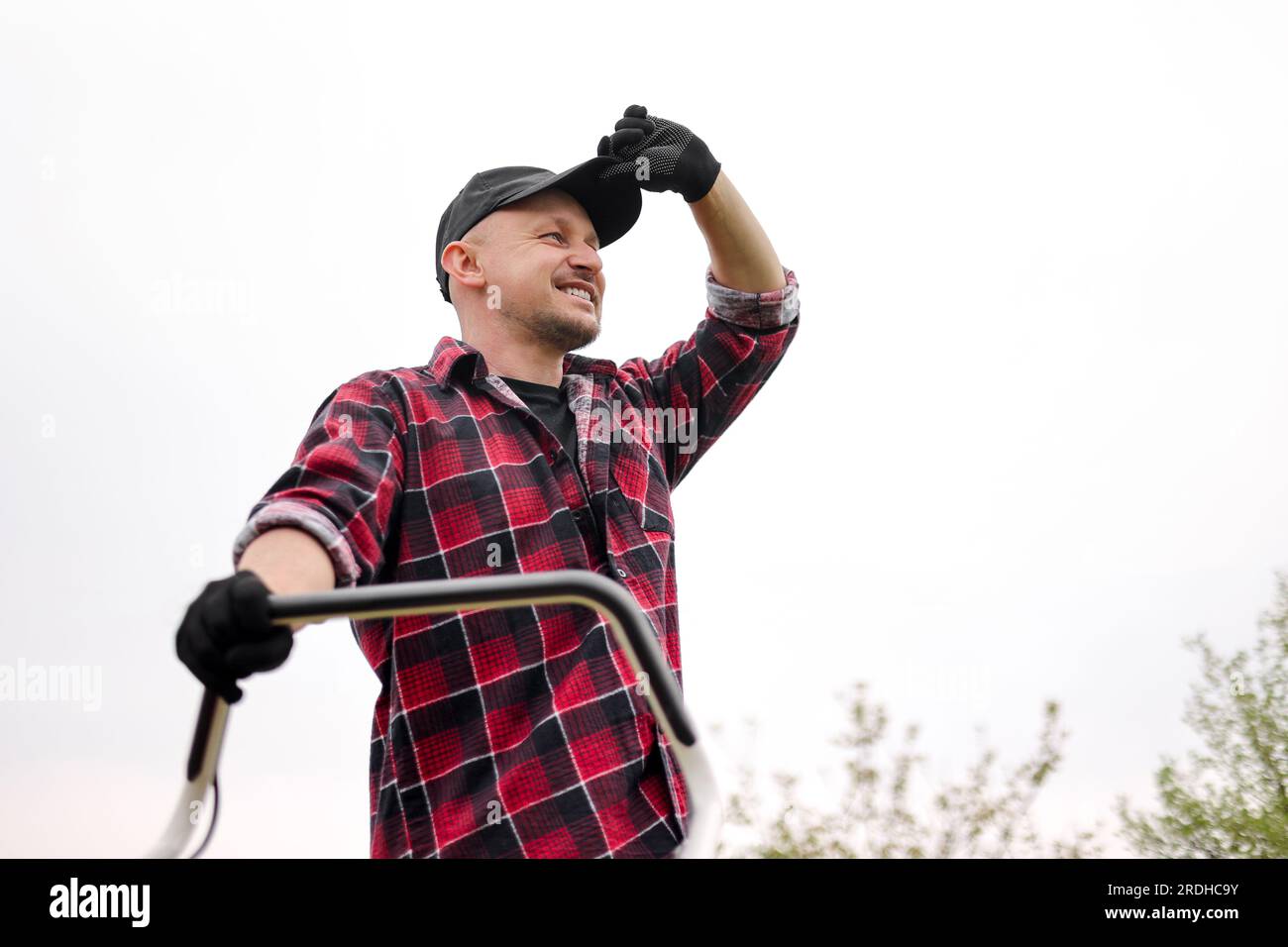 Bottom view of tired man makes a short break while cutting grass with a ...