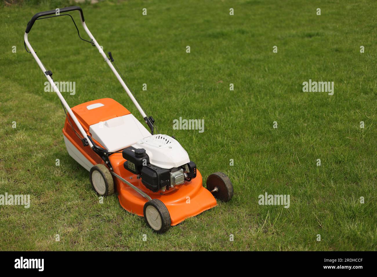Top view of modern orange-grey electric lawn mower cutting bright lush ...