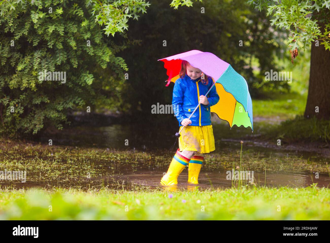 Little girl playing in rainy summer park. Child with colorful rainbow ...