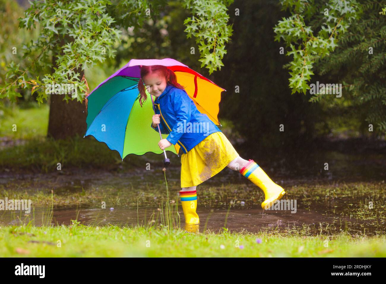 Little girl playing in rainy summer park. Child with colorful rainbow ...