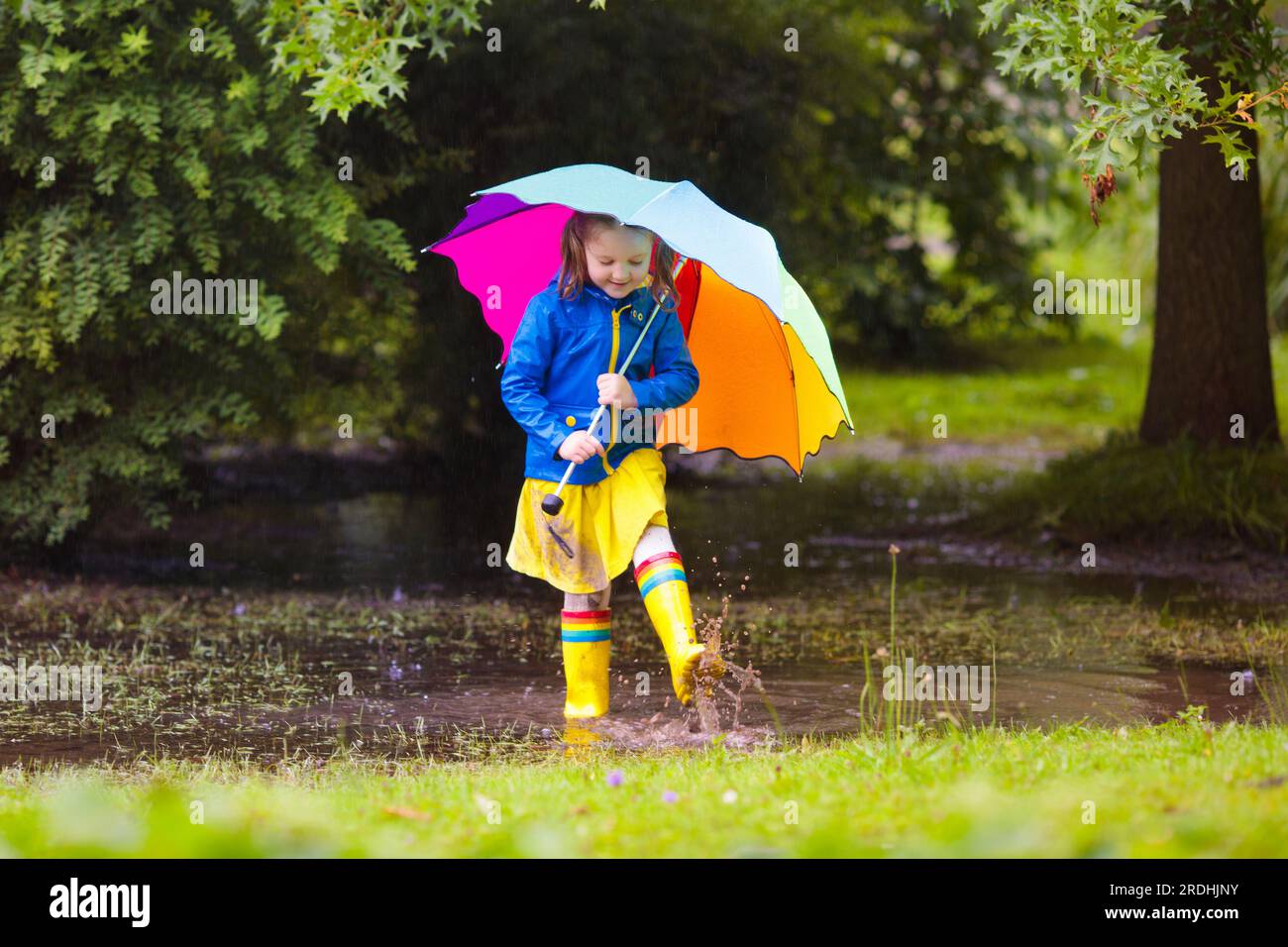 Little girl playing in rainy summer park. Child with colorful rainbow ...