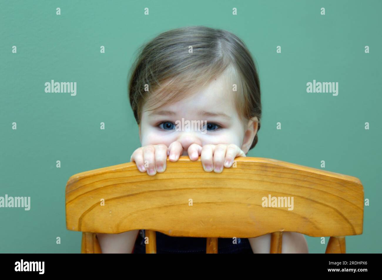 Toddler rests her head against her hands as she leans over the back of ...