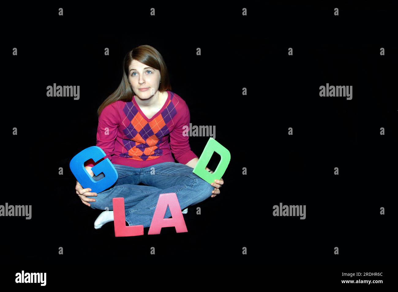 Young woman sits in an all black room holding the letters spelling ...