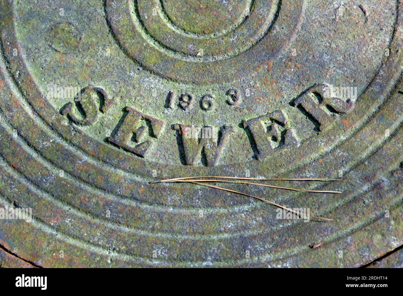 Sewer cover plate is heavy iron with ring design. The letters spelling ...