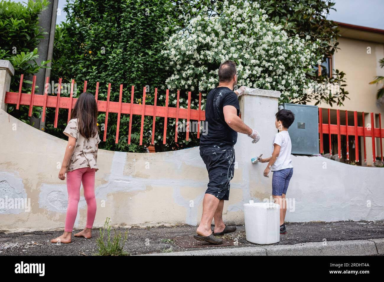 father with two daughters painting in white the old house fence Stock ...
