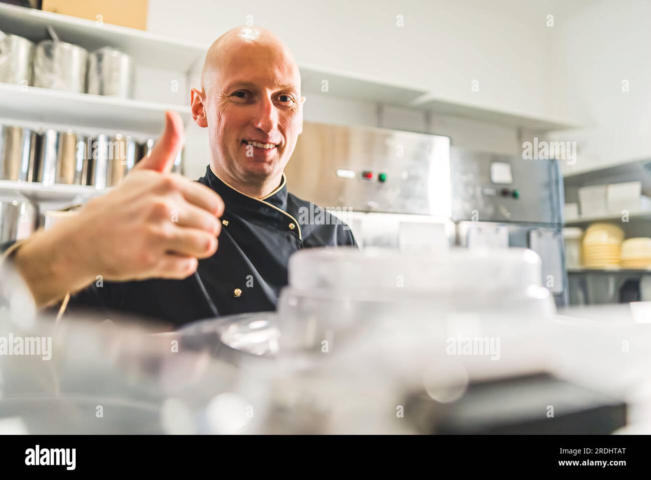 Pastry business owner with a thumbs up standing in cluttered kitchen ...