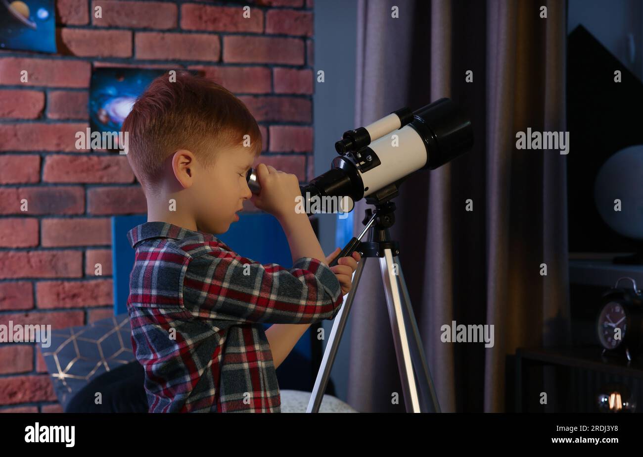 Little boy looking at stars through telescope in room Stock Photo - Alamy