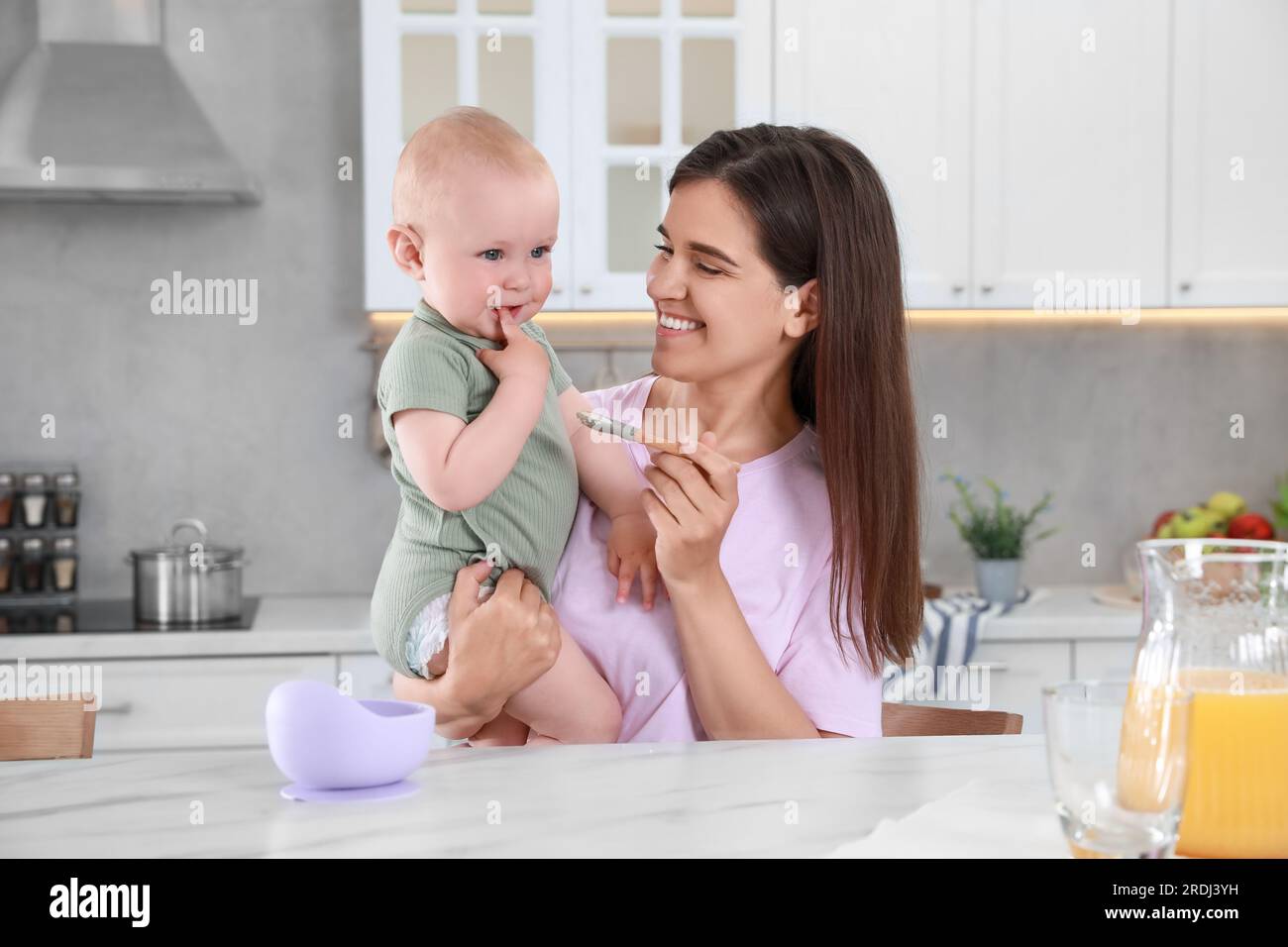 Happy young woman feeding her cute little baby at table in kitchen ...