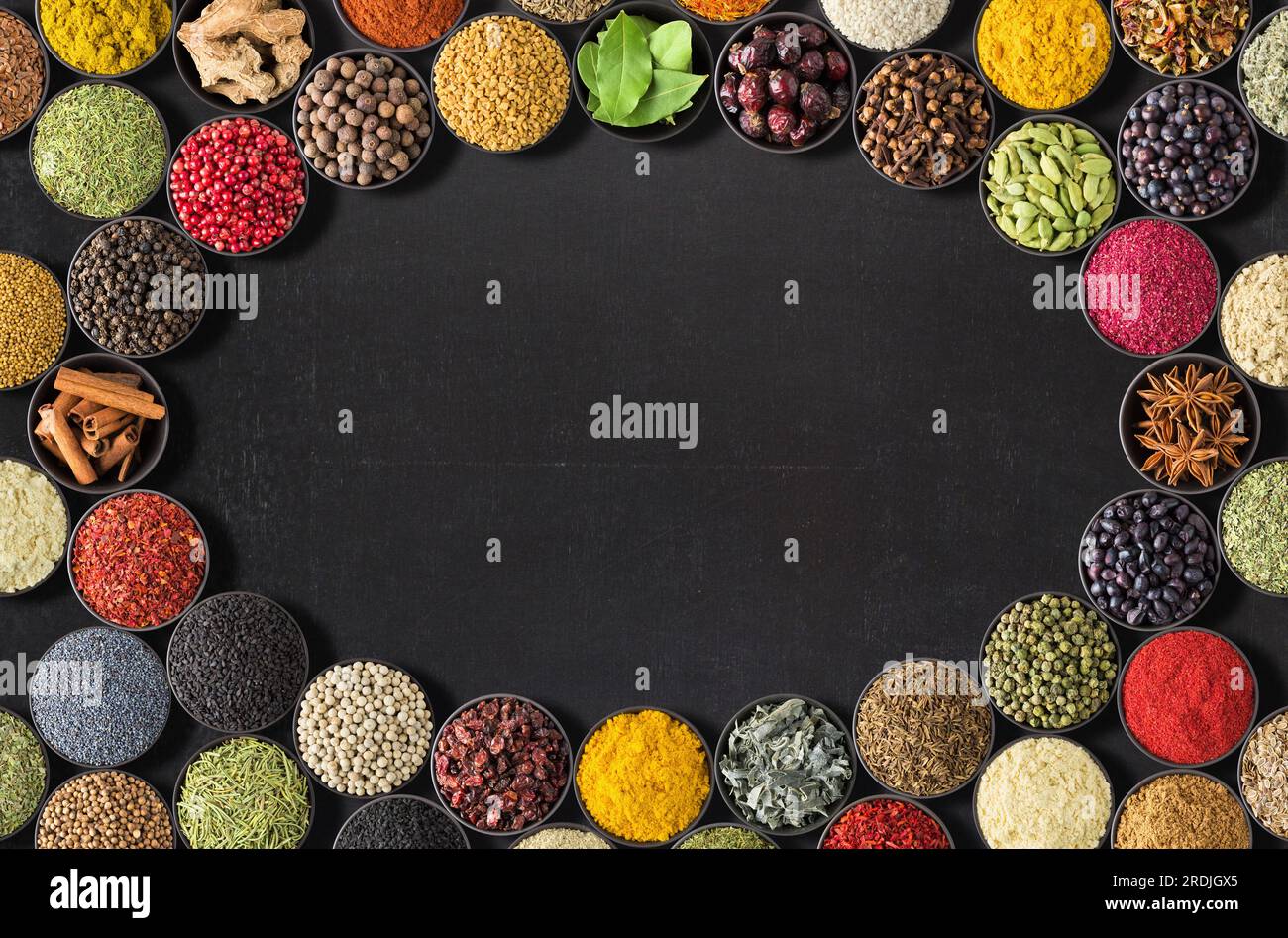 different condiments lie around. Indian spices and herbs on black table ...