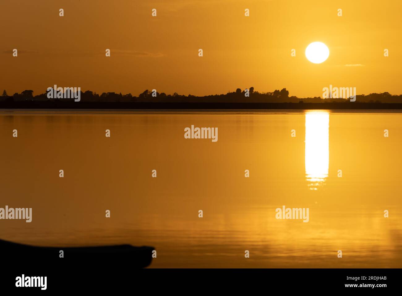 Golden sunrise with glow of round sun rising above horizon across bay ...