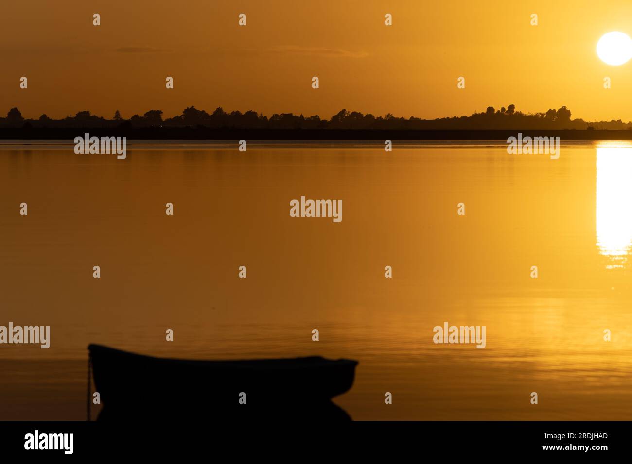 Golden sunrise with glow of round sun rising above horizon across bay ...