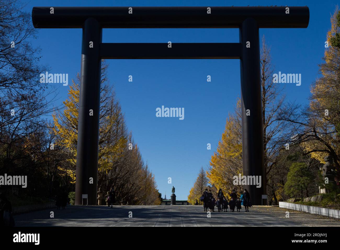 Mothers and kindergarten children walk under the large iron torii gate ...
