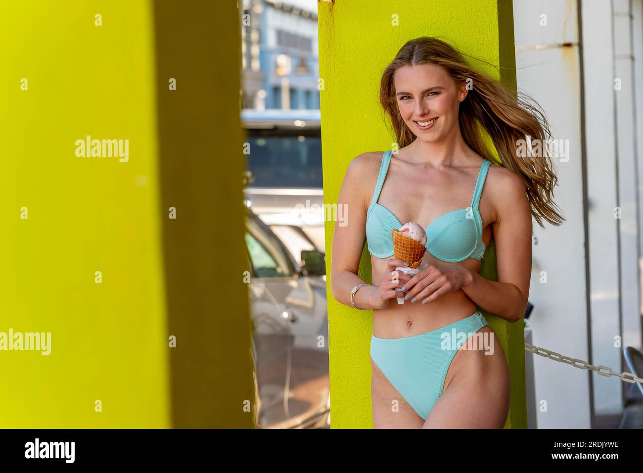 A gorgeous brunette bikini model enjoys an ice cream cone while relaxing in the spring weather ...