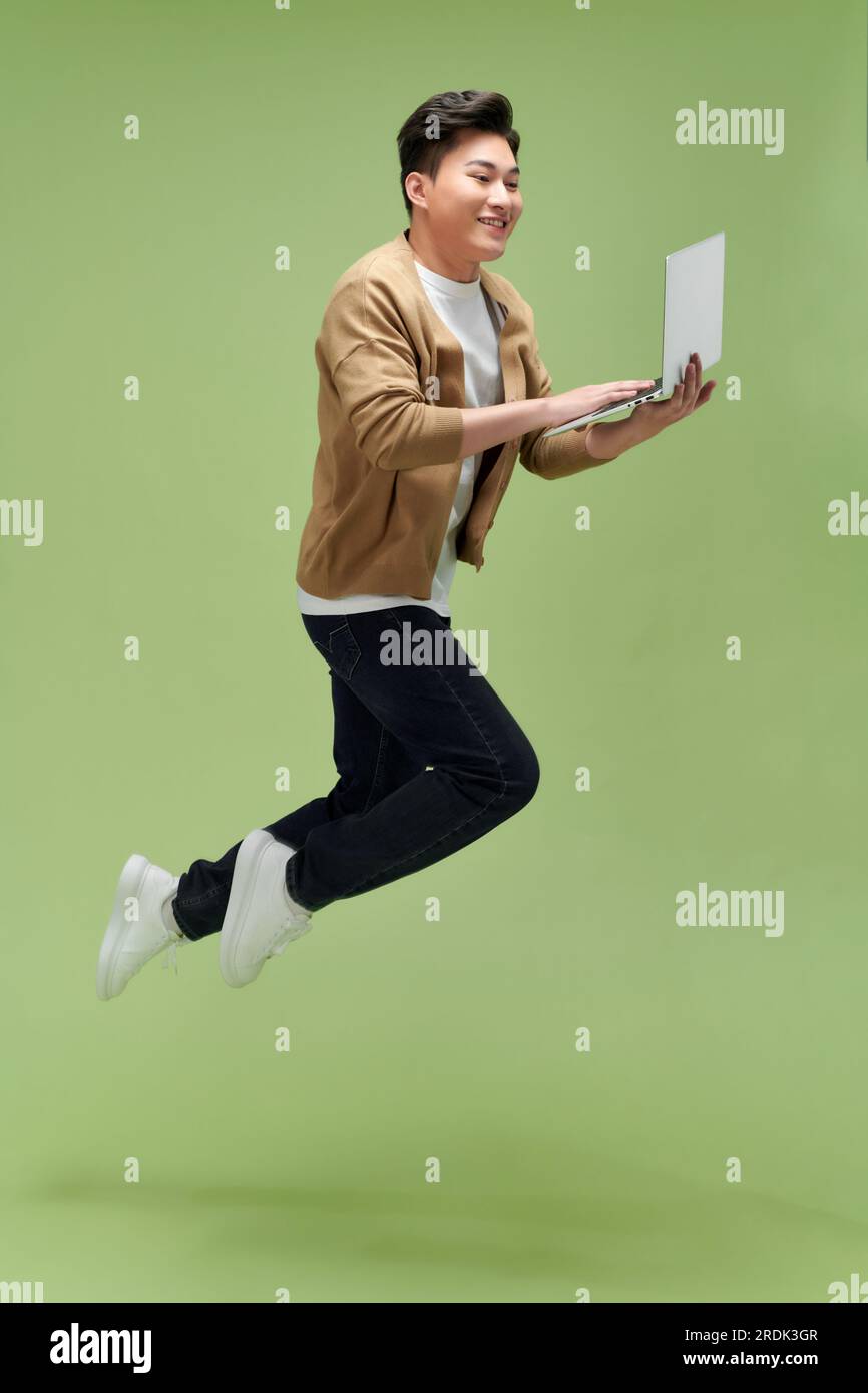Full length portrait of a happy young man jumping with laptop computer ...