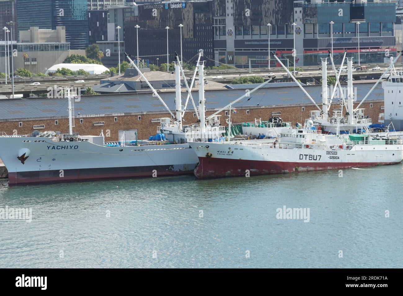 White refrigerated cargo ship and fishing vessel moored side by side in ...