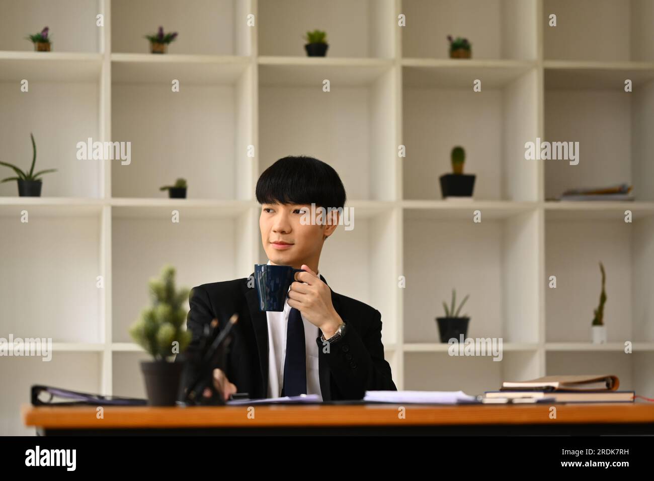 Thoughtful Asian male entrepreneur sitting at office desk and looking ... Thoughtful Asian male entrepreneur sitting at office desk and looking ...