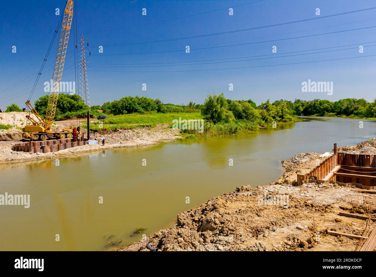 Across the water is yellow obsolete mobile crane with pneumatic hammer ...