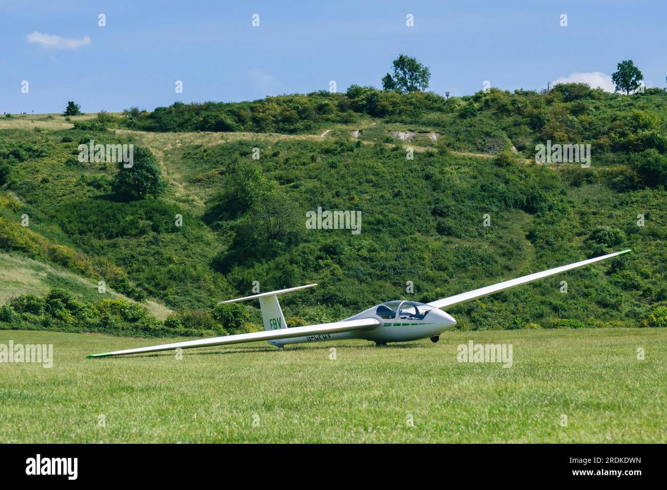 A glider sits beside the runway with its wing leaning on the ground at ...