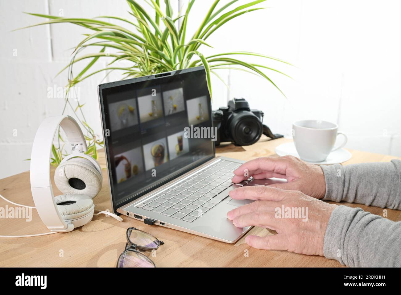 Hands typing on a laptop on a wooden desk with headphones, camera ...